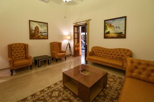 Uma sala de estar com um sofá, poltronas, uma mesa de centro e duas pinturas nas paredes.