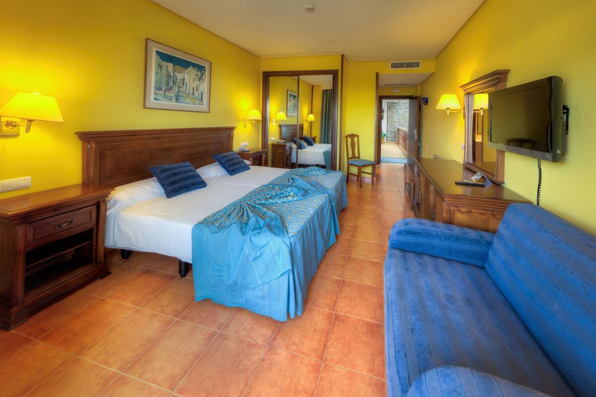 Quarto de hotel com duas camas, um sofá, uma televisão e um espelho.