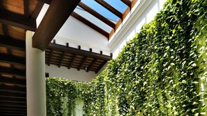 Um pátio coberto com piso de azulejos, teto de madeira e paredes decoradas com plantas trepadoras.