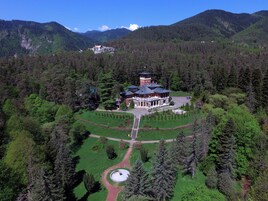 Um edifício grande e histórico com um pátio central, rodeado por uma floresta densa e montanhas.