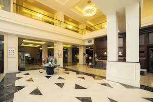Um hall amplo com teto alto, um lustre e um balcão de recepção.