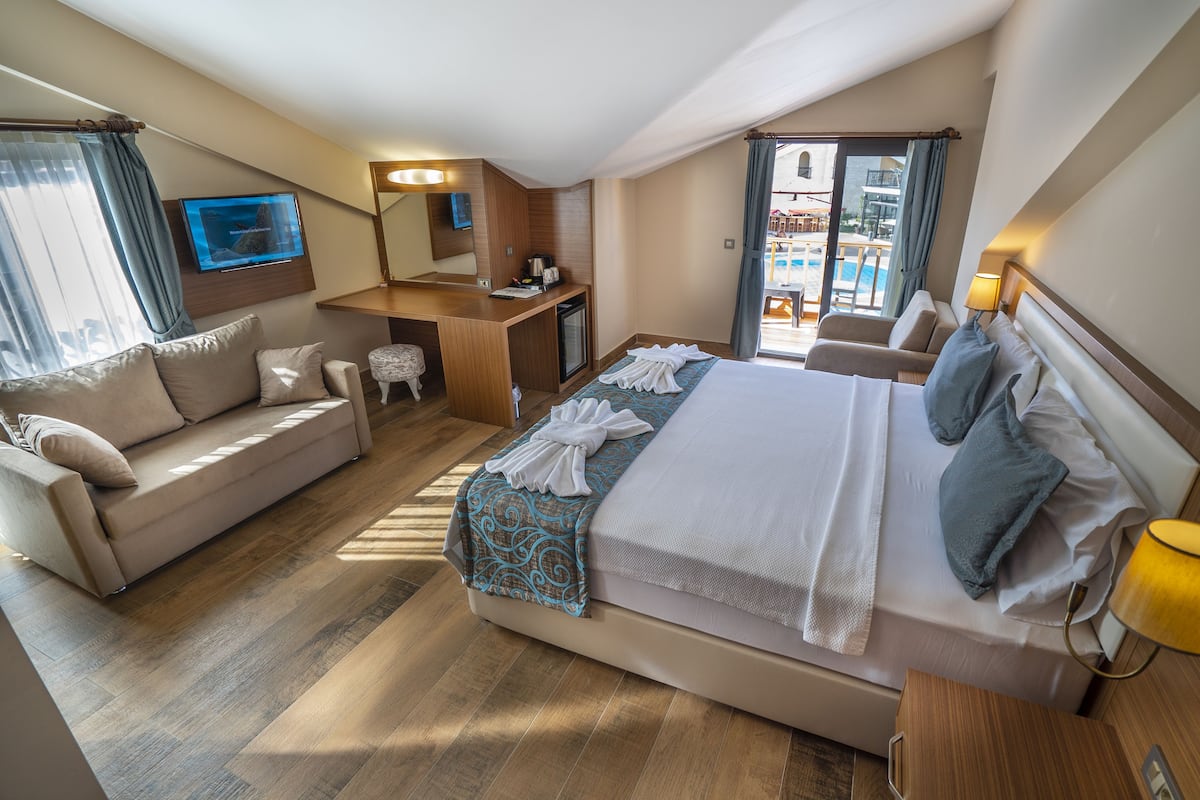 Quarto de hotel com cama, sofá, escrivaninha, televisão e varanda com piscina.