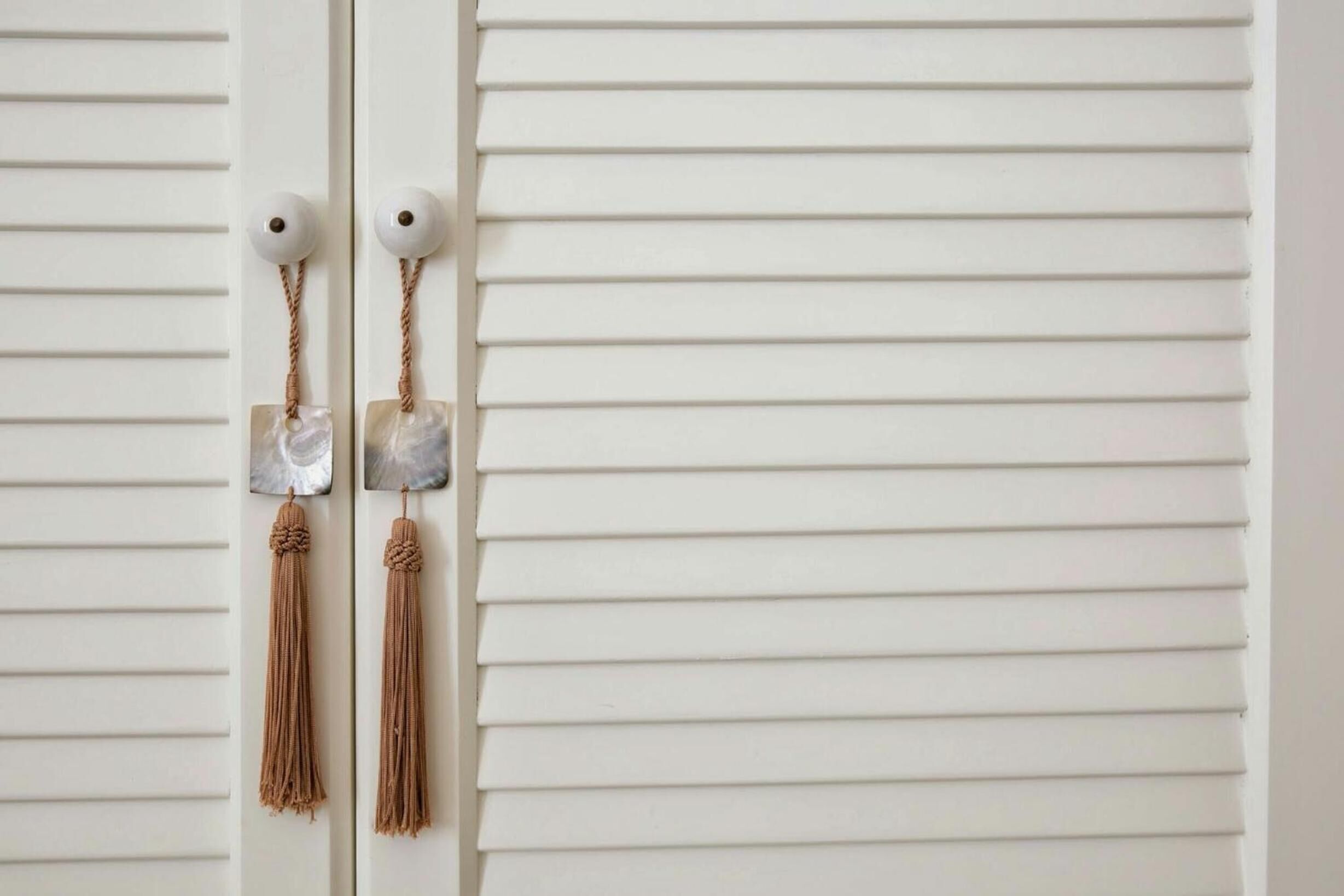 Uma porta branca com ripas horizontais e dois objetos decorativos pendurados nela.