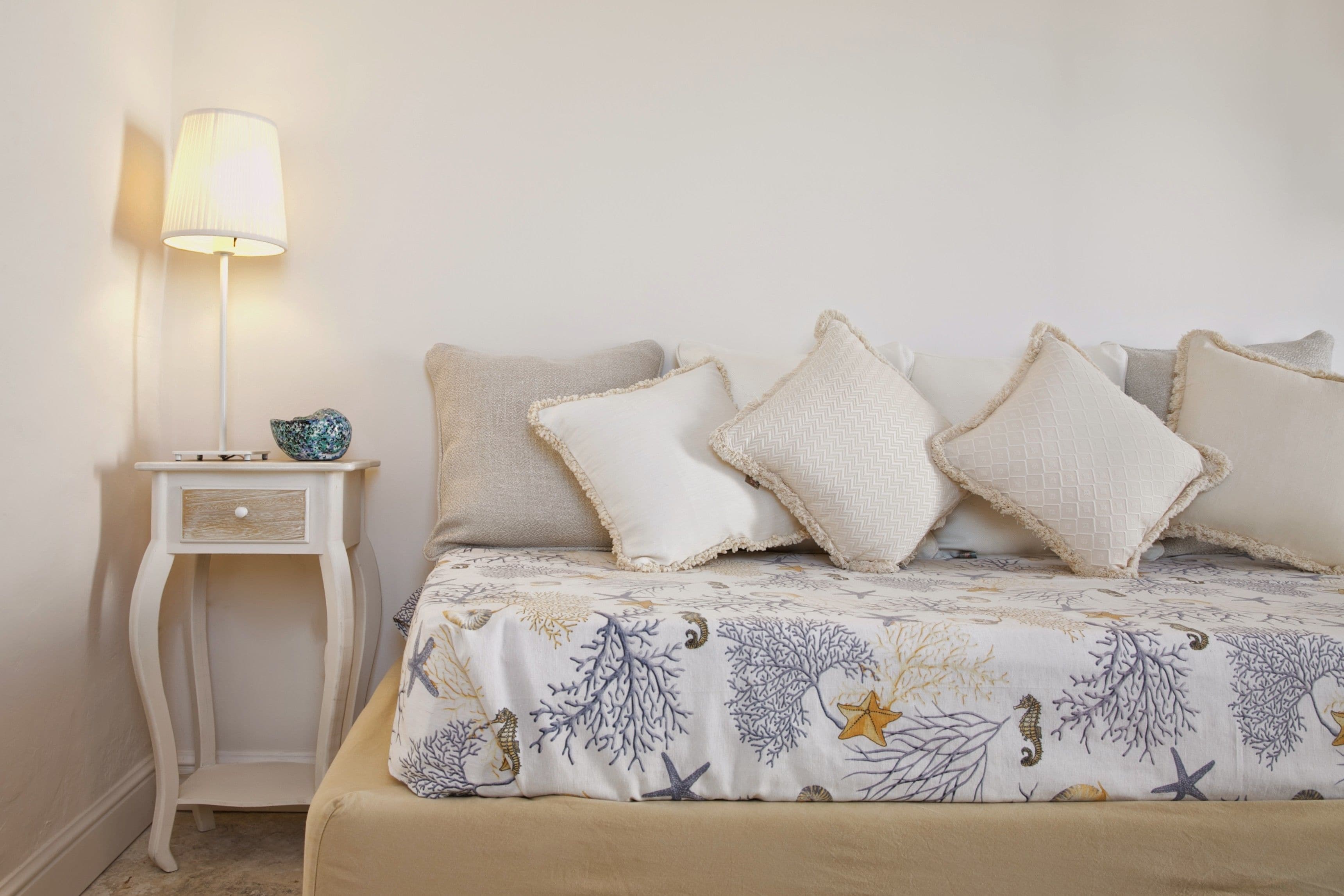 Uma cama com colcha estampada, mesa de cabeceira com abajur e vários travesseiros.