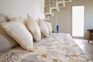 Quarto com cama coberta por uma colcha estampada, várias almofadas e uma escada ao fundo.