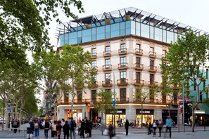 Um edifício moderno com fachada de vidro, rodeado por árvores e pedestres.