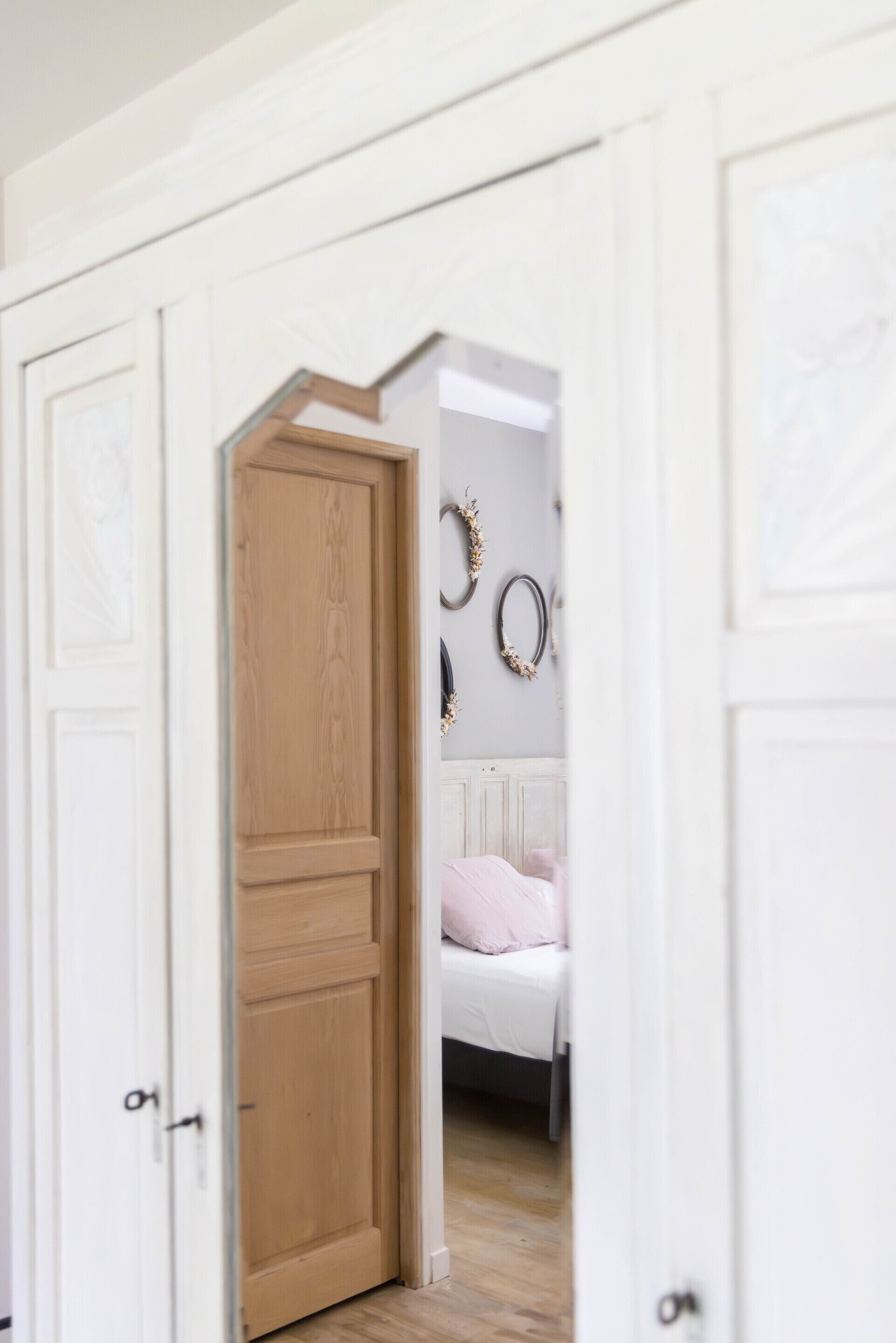 Um quarto com porta de madeira, cama com cabeceira branca e decoração na parede.