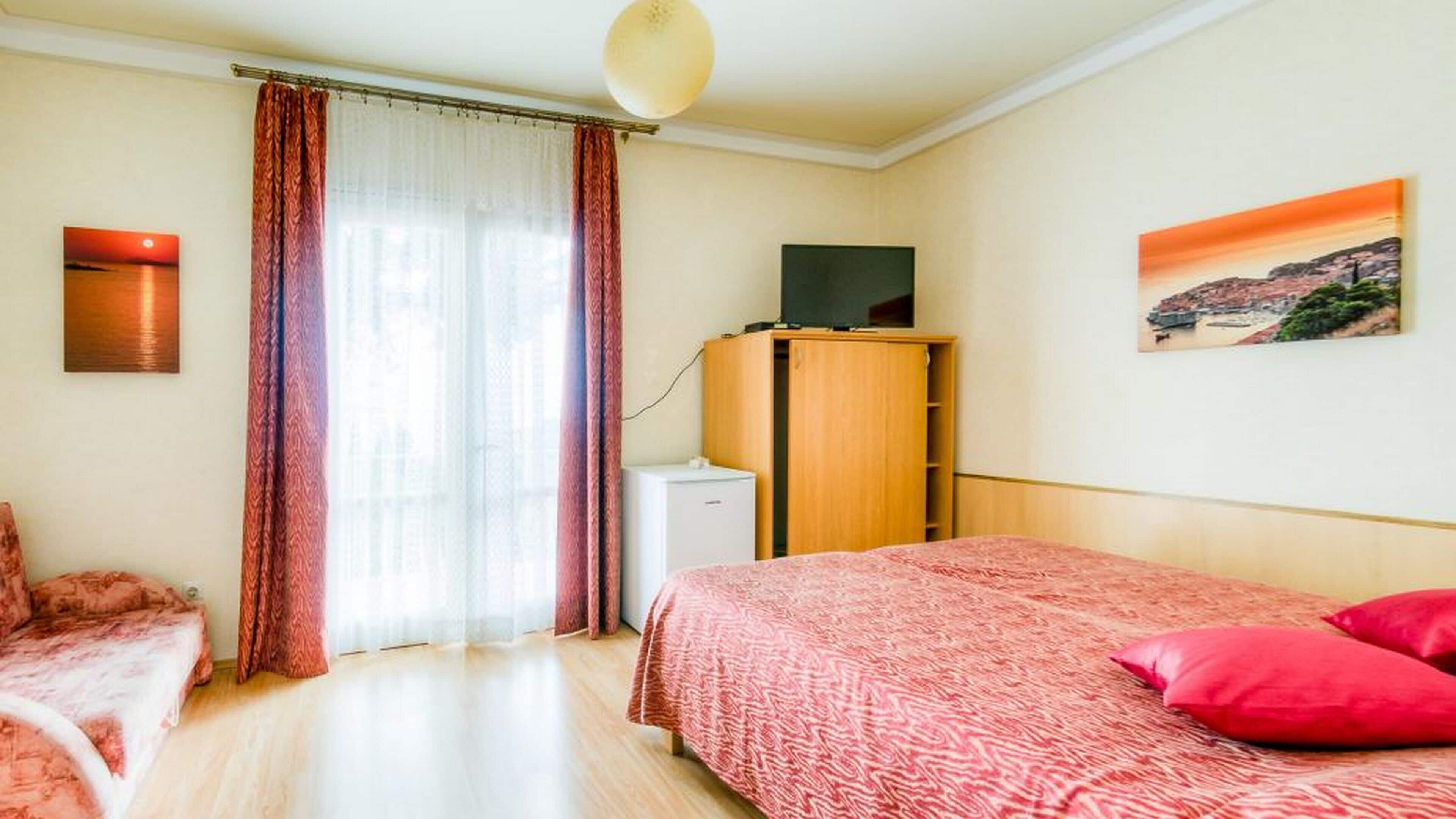 Quarto de hotel com cama, escrivaninha, cadeira, guarda-roupa, televisão e um quadro na parede.