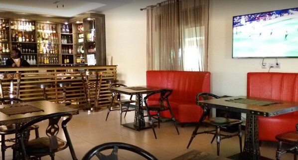 Uma área de bar com prateleiras de garrafas, uma televisão exibindo um evento esportivo e opções de assentos.