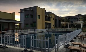 Um edifício moderno com piscina, cercado por uma vedação branca, área de estar ao ar livre e espaço coberto.