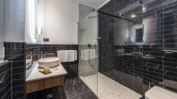 Casa de banho moderna com uma grande pia, chuveiro com divisória de vidro e azulejos de mármore preto.