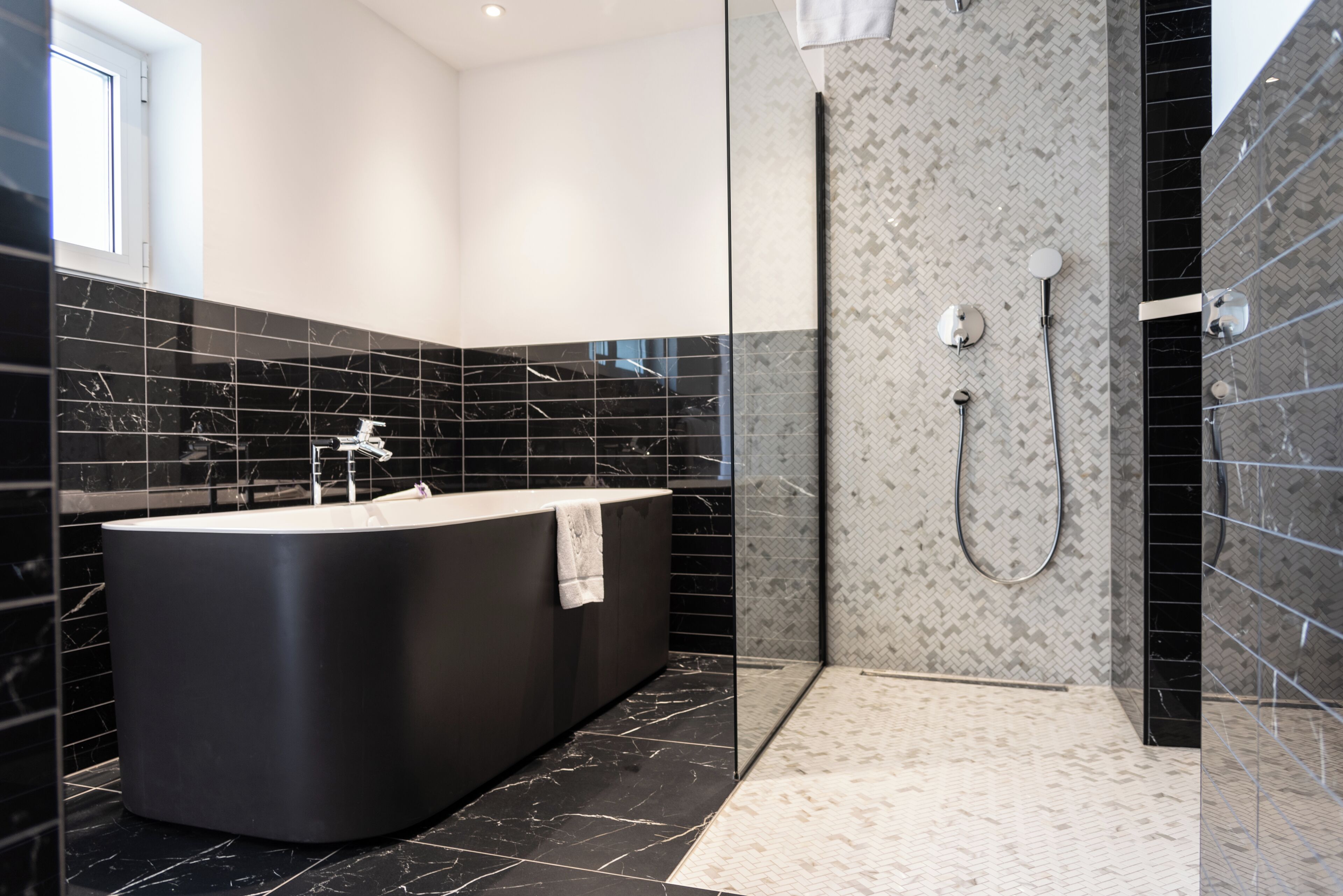 Uma casa de banho moderna com uma banheira independente, um chuveiro com proteção de vidro e um painel de azulejos em padrão herringbone.