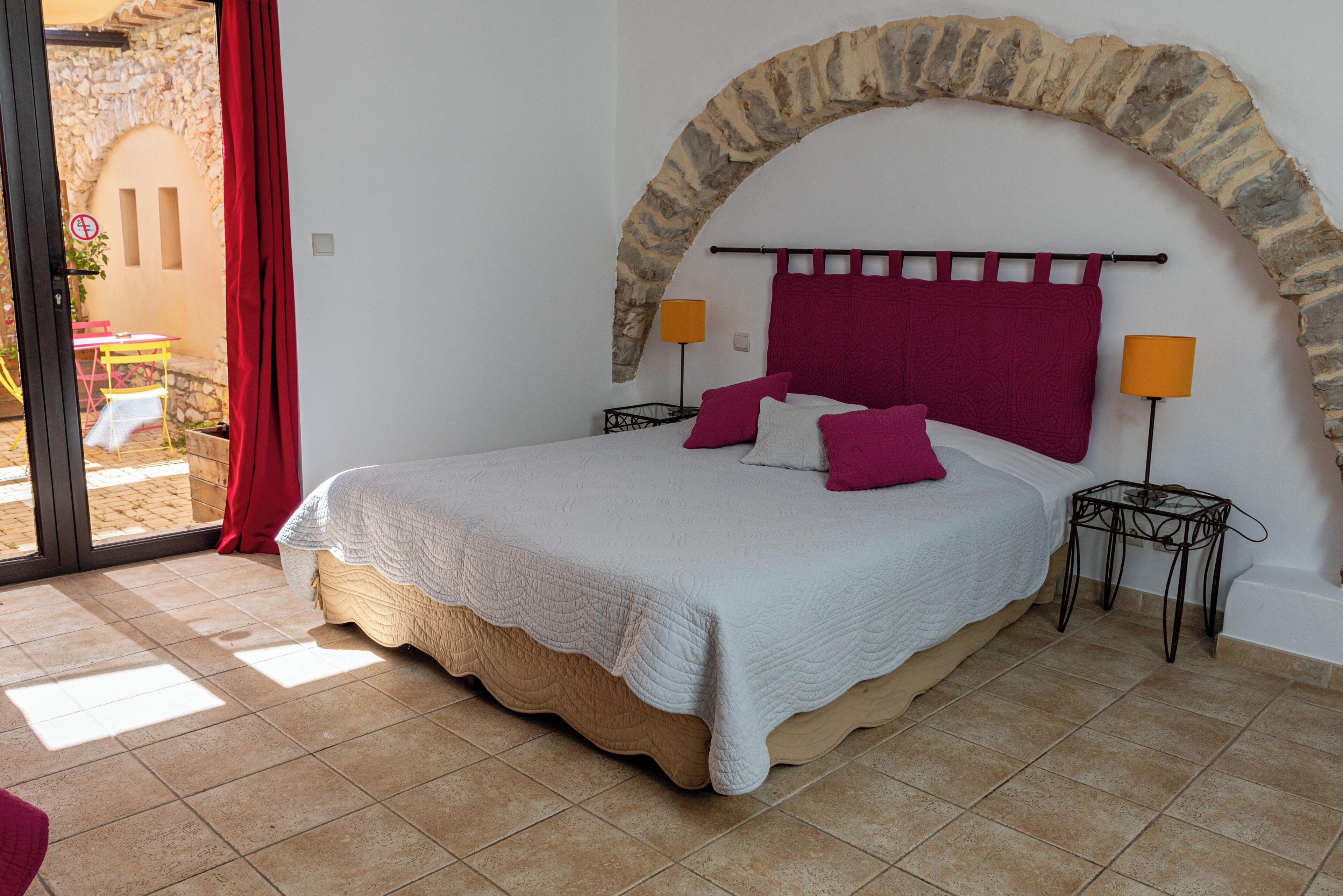 Quarto com arco de pedra sobre a cama, colcha branca e duas luminárias laterais.