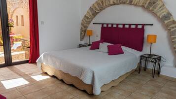 Quarto com arco de pedra sobre a cama, colcha branca e duas luminárias laterais.