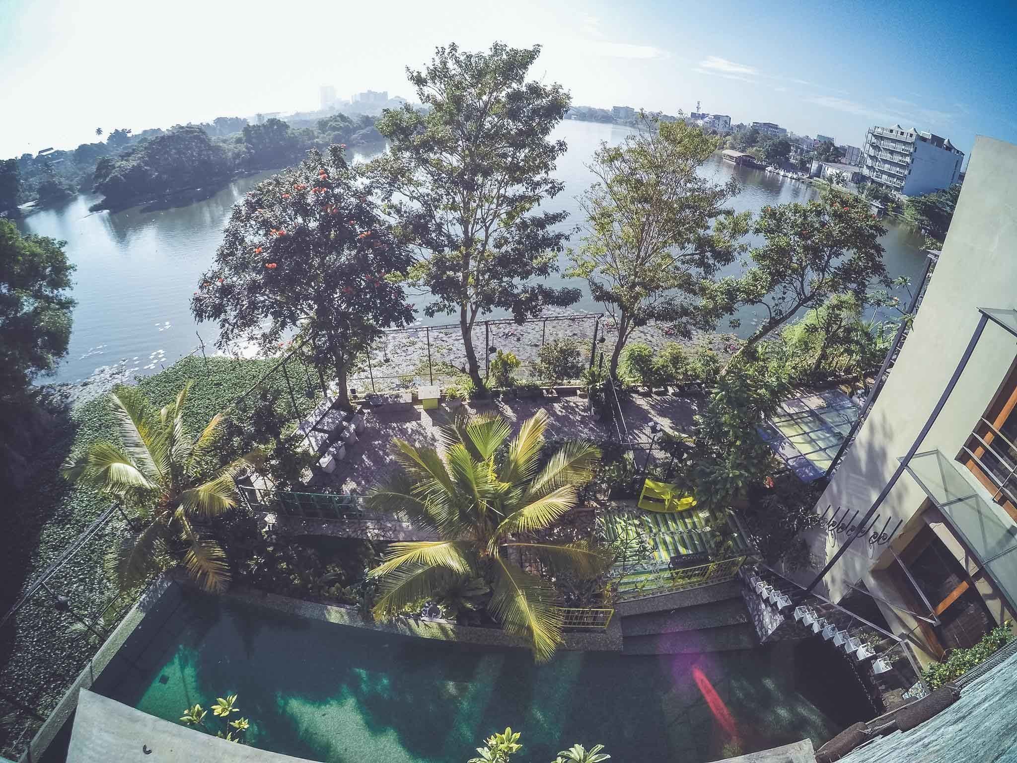 Vista de uma piscina rodeada por vegetação exuberante e um horizonte urbano ao fundo.