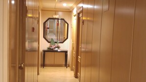 Um corredor com piso de madeira, um espelho na parede e uma pequena mesa com um vaso de flores.