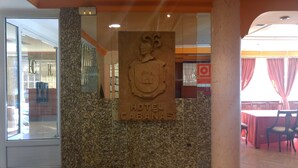 Entrada de um hotel com fachada de pedra, um brasão e uma placa com a inscrição "HOTEL CABANAS".