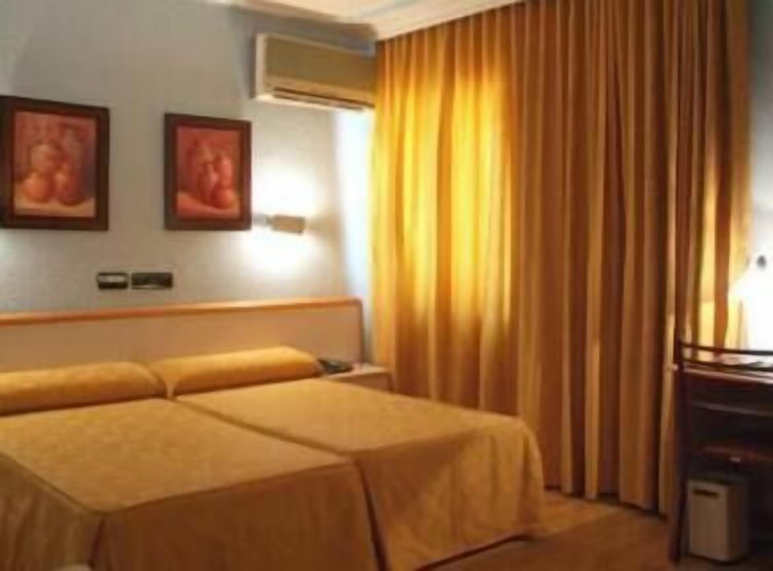 Quarto de hotel com uma cama de casal, uma escrivaninha, uma cadeira e janela com cortinas.