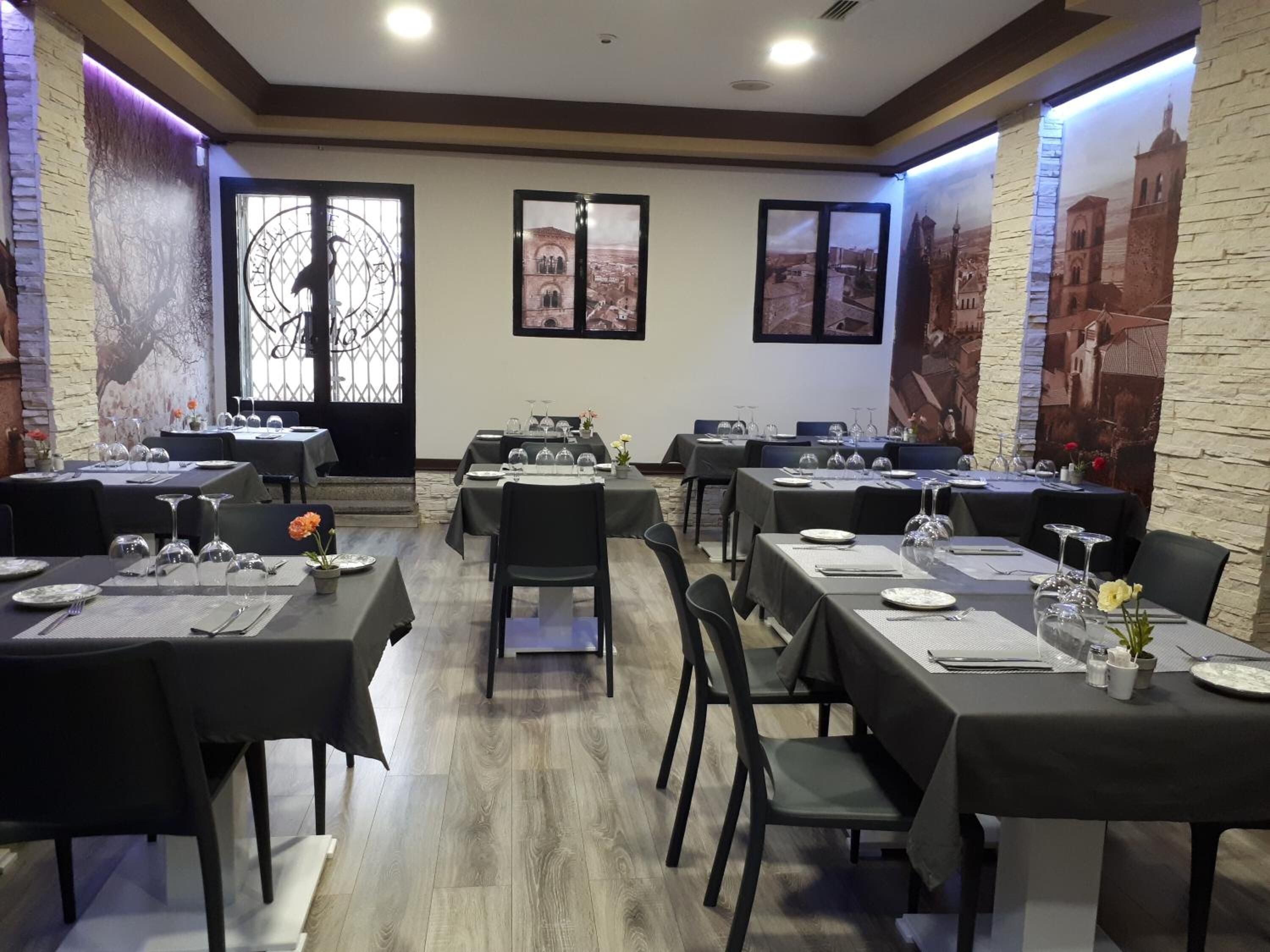 Um restaurante com várias mesas preparadas para refeições, apresentando um interior moderno com piso de madeira e cadeiras pretas.