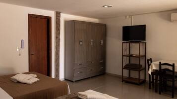 Quarto de hotel com duas camas, um guarda-roupa, uma televisão sobre um suporte e uma pequena mesa com cadeiras.