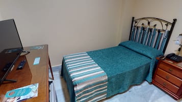Um quarto com uma cama, uma escrivaninha com um laptop, um telefone e uma mesinha de cabeceira.