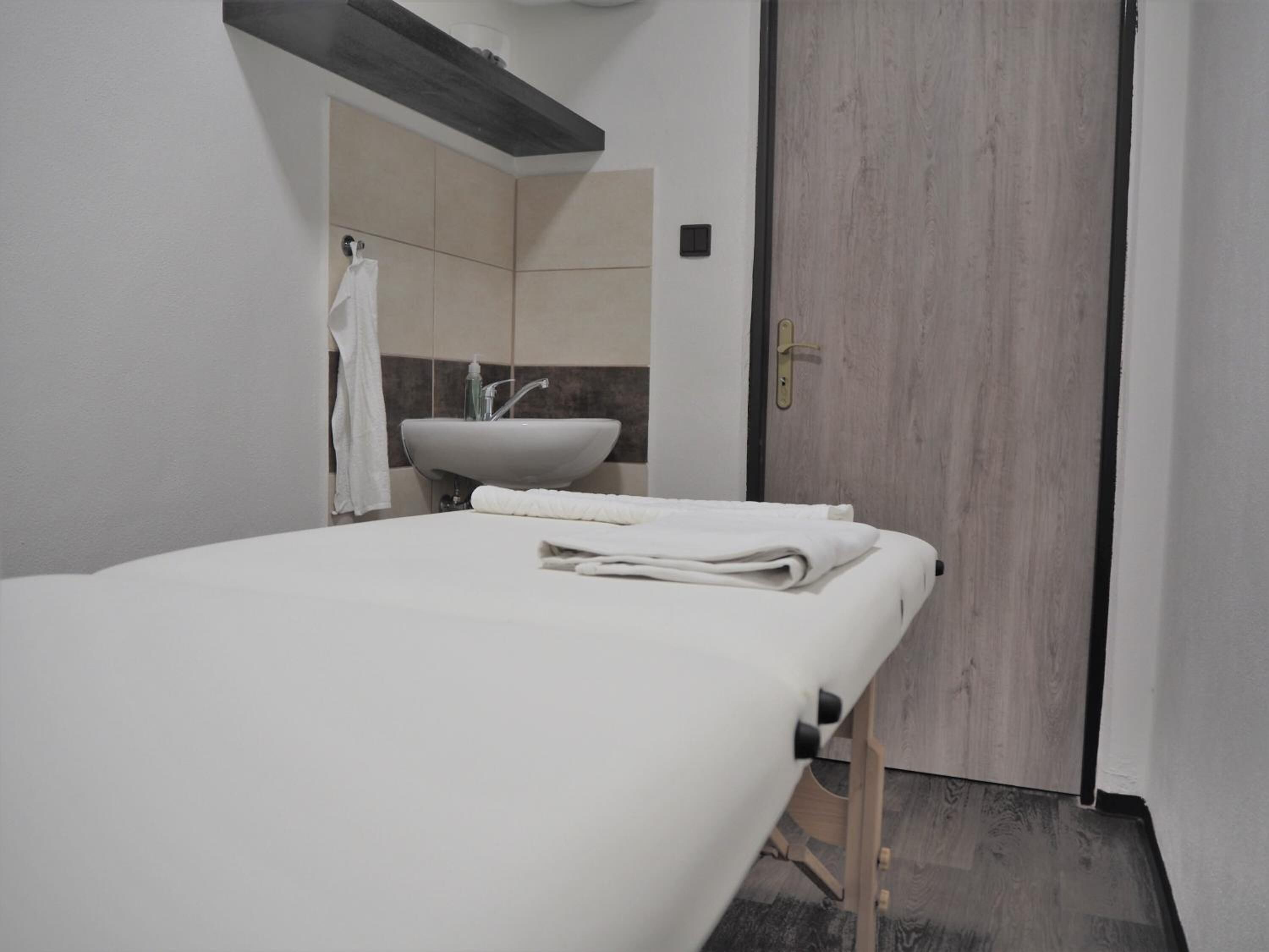 Um quarto com uma cama, uma mesa de cabeceira, uma pia branca e uma porta.