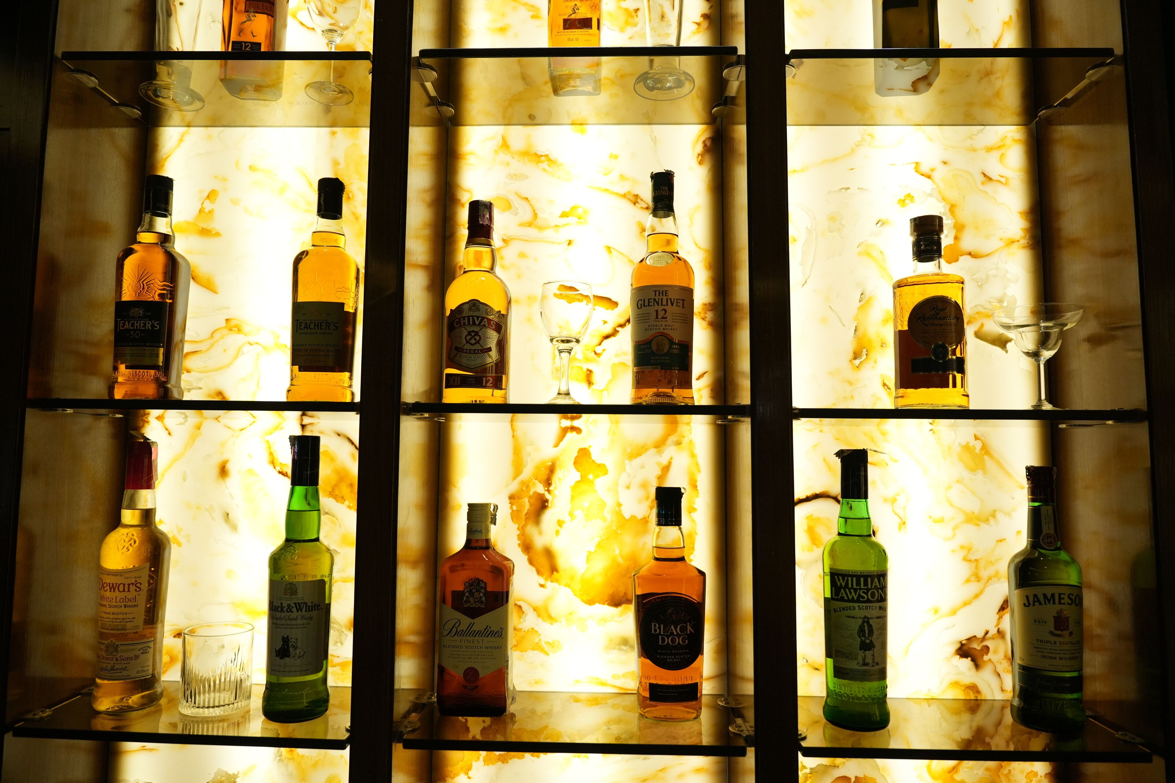 Uma área de bar com prateleiras repletas de garrafas de bebidas e copos.