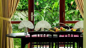 Uma área de refeições com uma mesa posta para dois, uma janela com vista para vegetação exuberante, e uma placa com a inscrição "The Francis Residence".