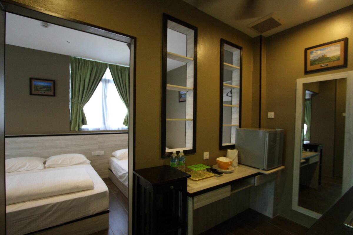 Quarto de hotel com cama, escrivaninha com micro-ondas, espelho e janela com cortinas.
