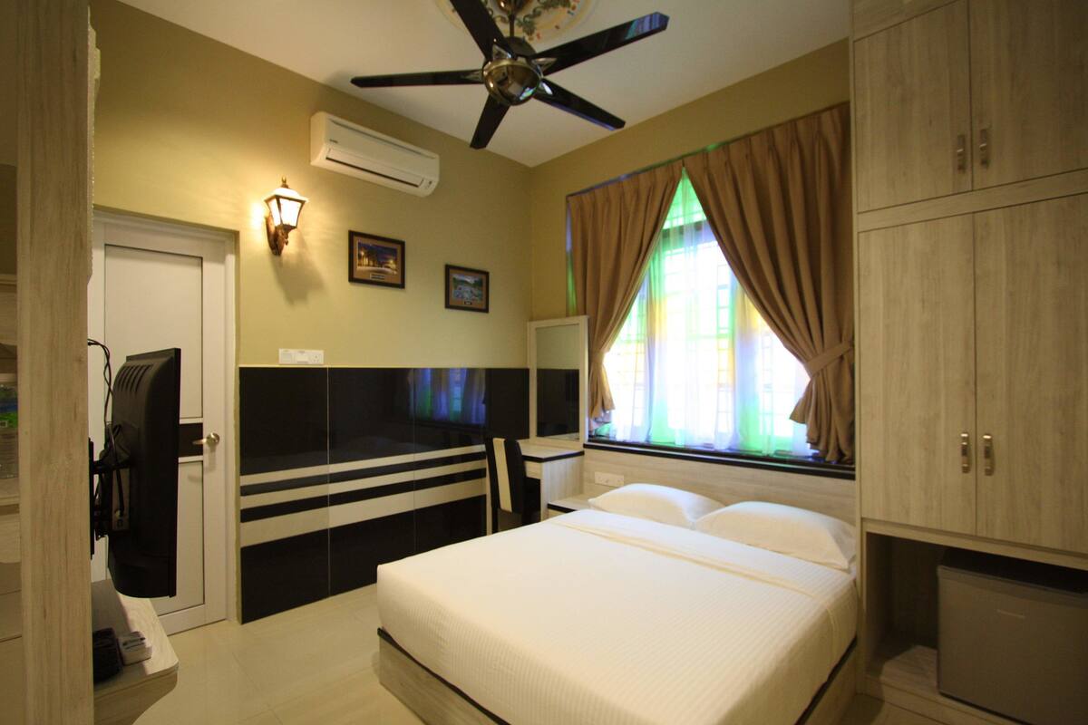 Quarto de hotel com cama, escrivaninha, cadeira, televisão e guarda-roupa.