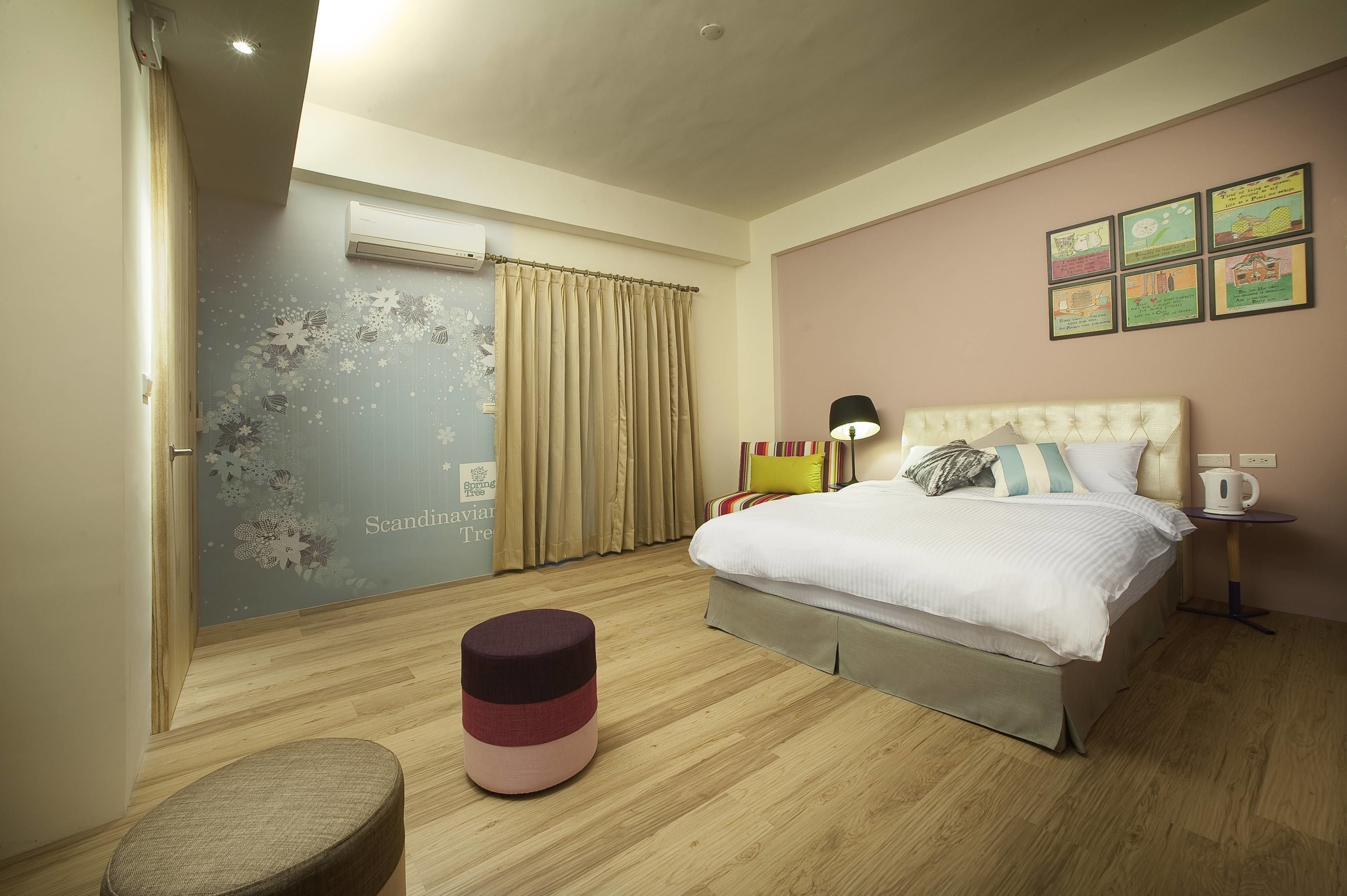Quarto com cama, mesa de cabeceira, abajur, mesinha com chaleira e parede com quadros.
