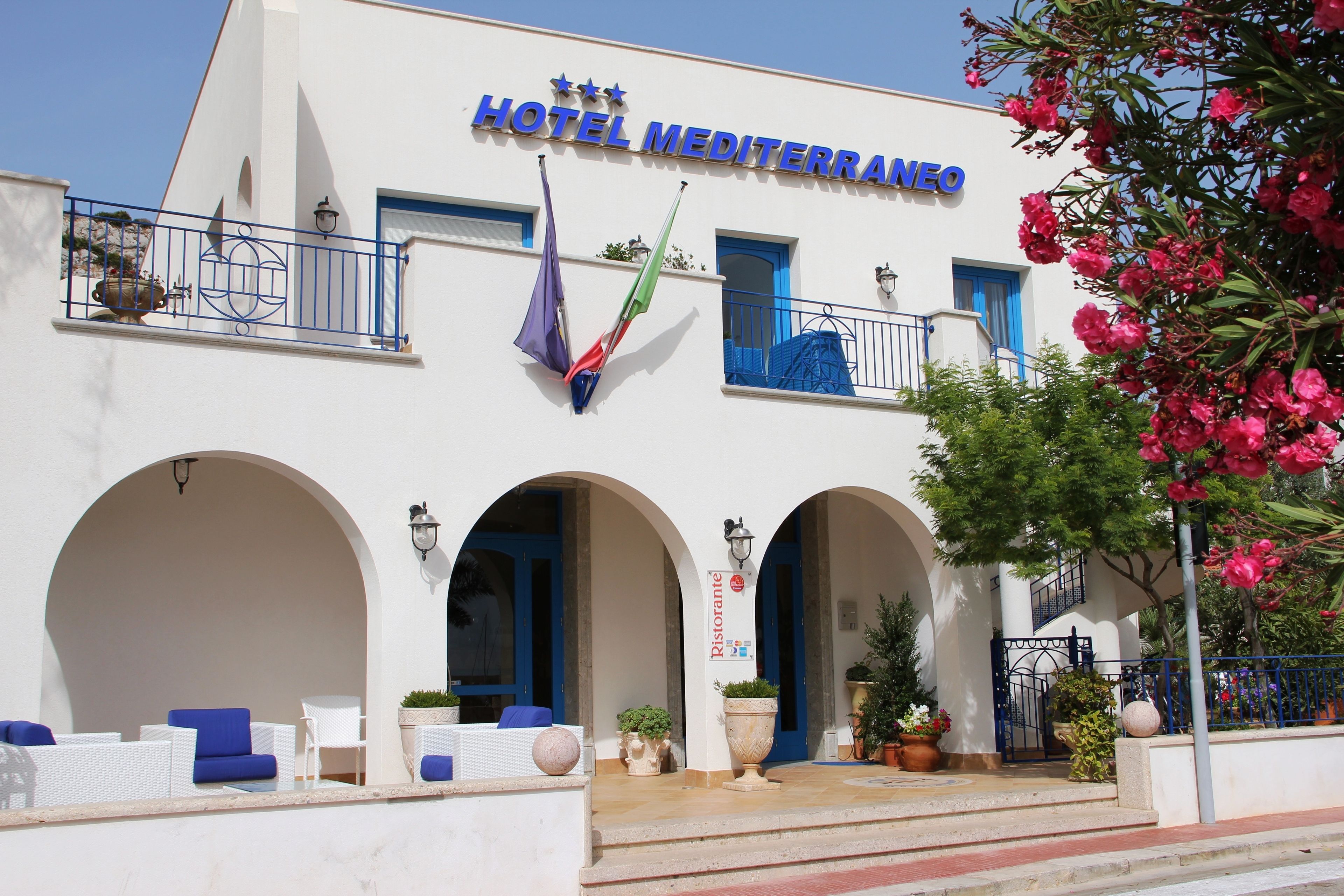 Um hotel com fachada branca, detalhes em azul e área de estar externa.