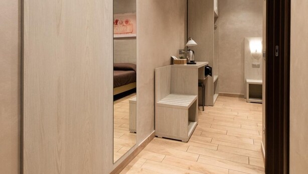 Um corredor moderno com piso de madeira, guarda-roupa espelhado, mesa de cabeceira com abajur e um pequeno espaço de estar.