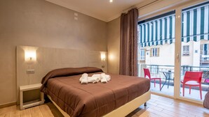 Quarto de hotel com cama, mesa de cabeceira, janela com cortinas e vista para a varanda externa.