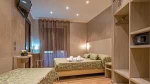 Quarto de hotel com duas camas, uma pequena escrivaninha com cadeira, um guarda-roupa e televisão na parede.