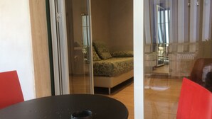 Quarto com uma cama, porta de vidro que dá para outro espaço e uma mesa com uma cadeira.