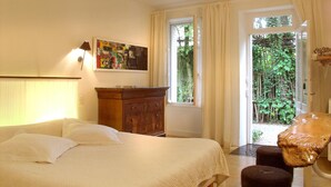 Quarto com uma cama, penteadeira de madeira, pintura e vista para o verde pela janela.
