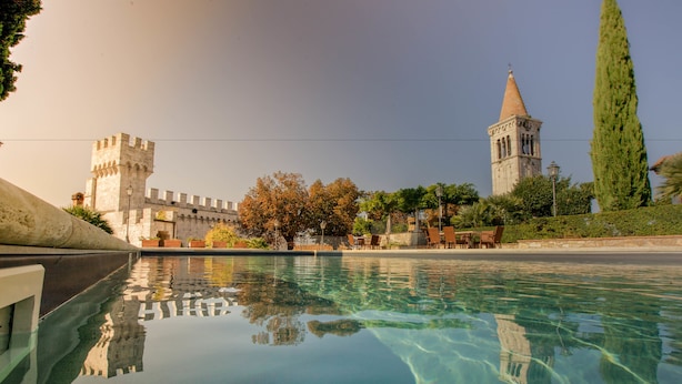 Piscina translúcida com um castelo e torre ao fundo.