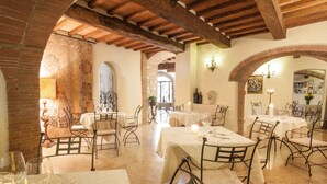 Um restaurante com várias mesas e cadeiras, com vigas de madeira aparente e arcos de tijolo.