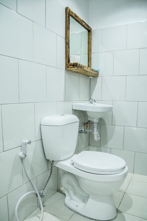 Um banheiro com azulejos brancos, vaso sanitário branco, pia e espelho com moldura de madeira.