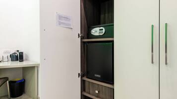 Quarto com porta branca, pequena escrivaninha com chaleira, lixeira e armário preto com puxador verde.