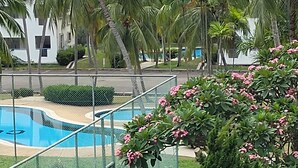 Uma área de piscina cercada, com um caminho, um poste de luz e um arbusto com flores rosa.