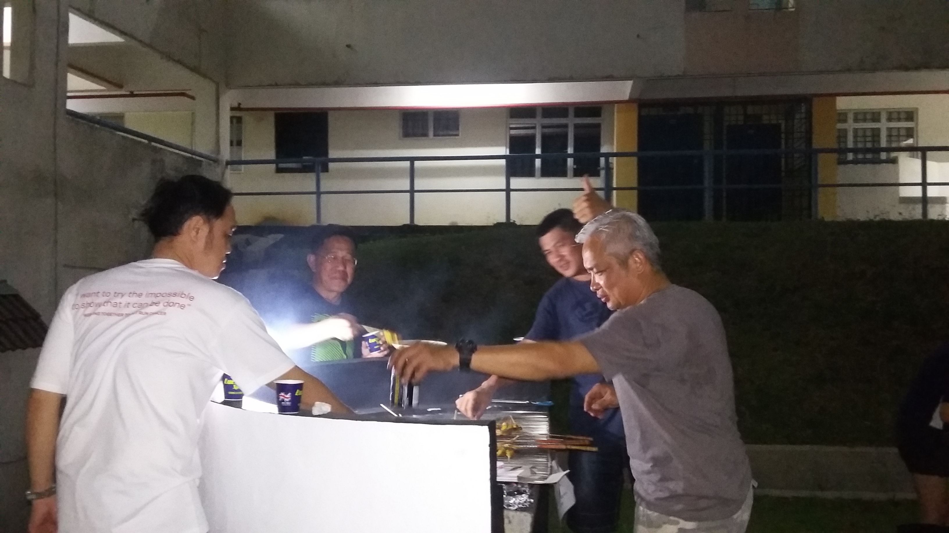 Um grupo de pessoas ao redor de uma mesa com churrasqueira, possivelmente preparando comida ao ar livre.