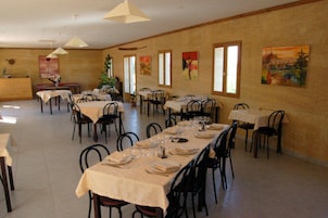 Uma sala de jantar com várias mesas postas, cadeiras e luminárias pendentes.