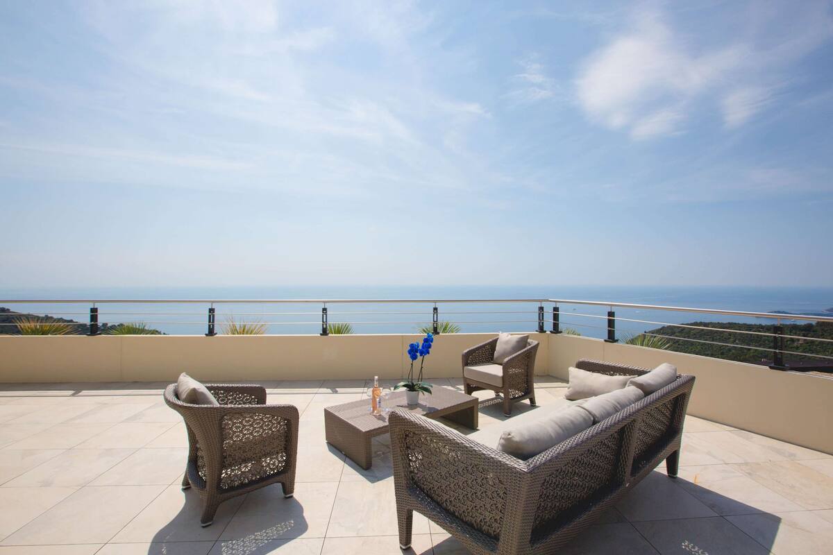 Um terraço com mobiliário de vime, uma mesa e vista para o mar.
