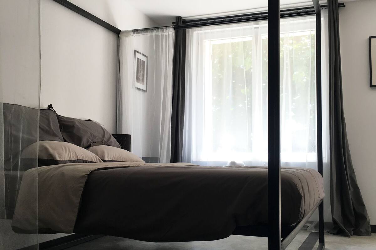 Quarto moderno com cama em separação de vidro, uma janela grande com cortinas e design minimalista.