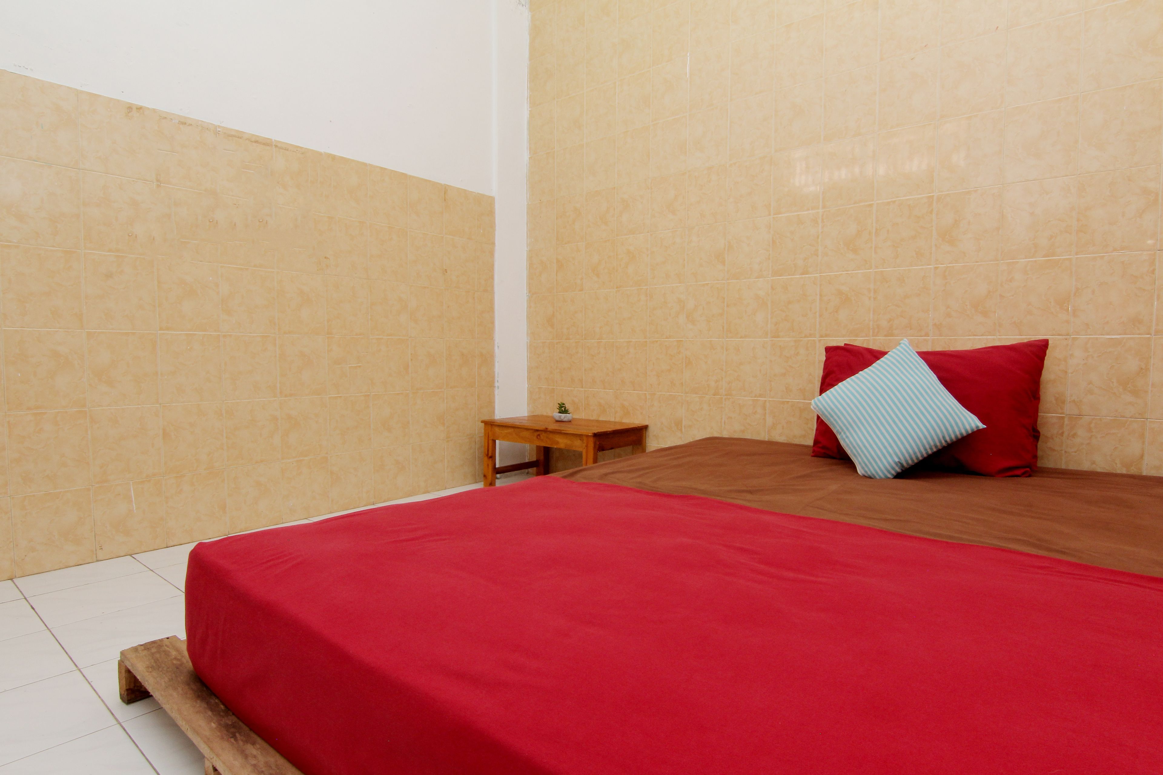 Quarto com cama de madeira, uma mesinha de cabeceira de madeira e almofada vermelha e azul.