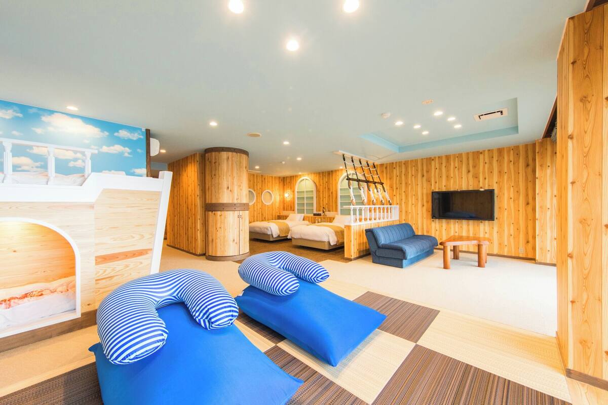 Quarto com cama, televisão, sofá azul e mesa de massagem com almofadas azuis.