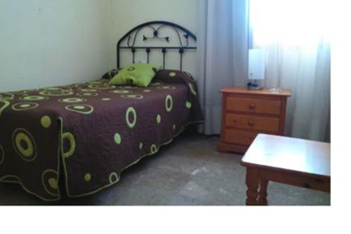 Um quarto com uma cama de solteiro, uma mesinha de cabeceira de madeira e um aparador.
