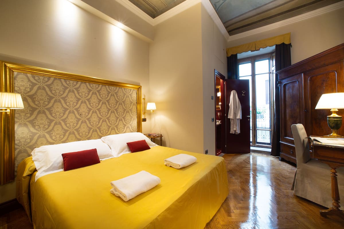 Quarto de hotel com uma cama grande, uma escrivaninha de madeira e uma cadeira.
